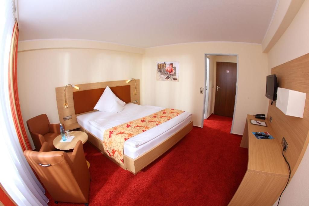 Quarto de hotel com cama, escrivaninha, cadeira e televisão.