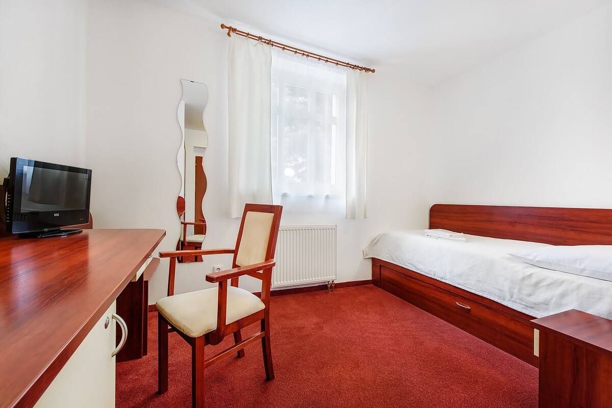 Quarto de hotel com uma escrivaninha de madeira, uma cadeira, uma cama e uma televisão.