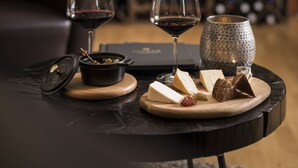 Uma mesa com queijo, uvas e copos de vinho, com estantes de vinho ao fundo.