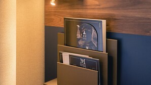 Uma luminária moderna fixada na parede com cúpula texturizada, um painel de madeira e um porta-revistas com logotipo.