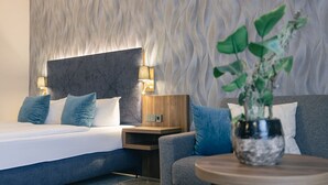 Quarto de hotel moderno com cama, mesas de cabeceira, um sofá e uma planta decorativa.