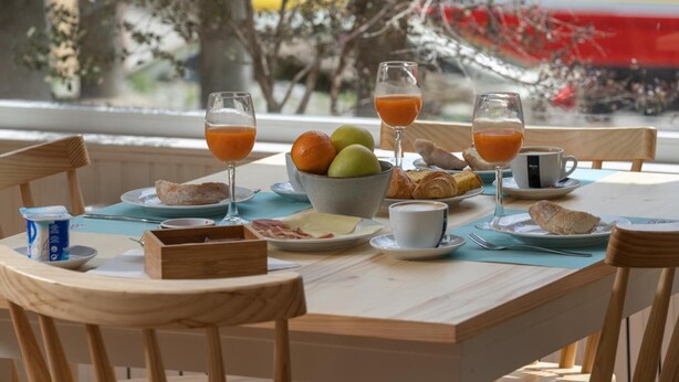 Uma mesa de café da manhã com uma tigela de frutas, croissants e copos de suco de laranja.