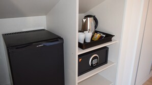 Uma cozinha compacta com geladeira preta, cafeteira e bandeja com xícaras e lanche.