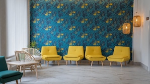 Quarto com papel de parede azul floral, quatro cadeiras amarelas, uma cadeira de vime, uma mesa de madeira e um lustre.