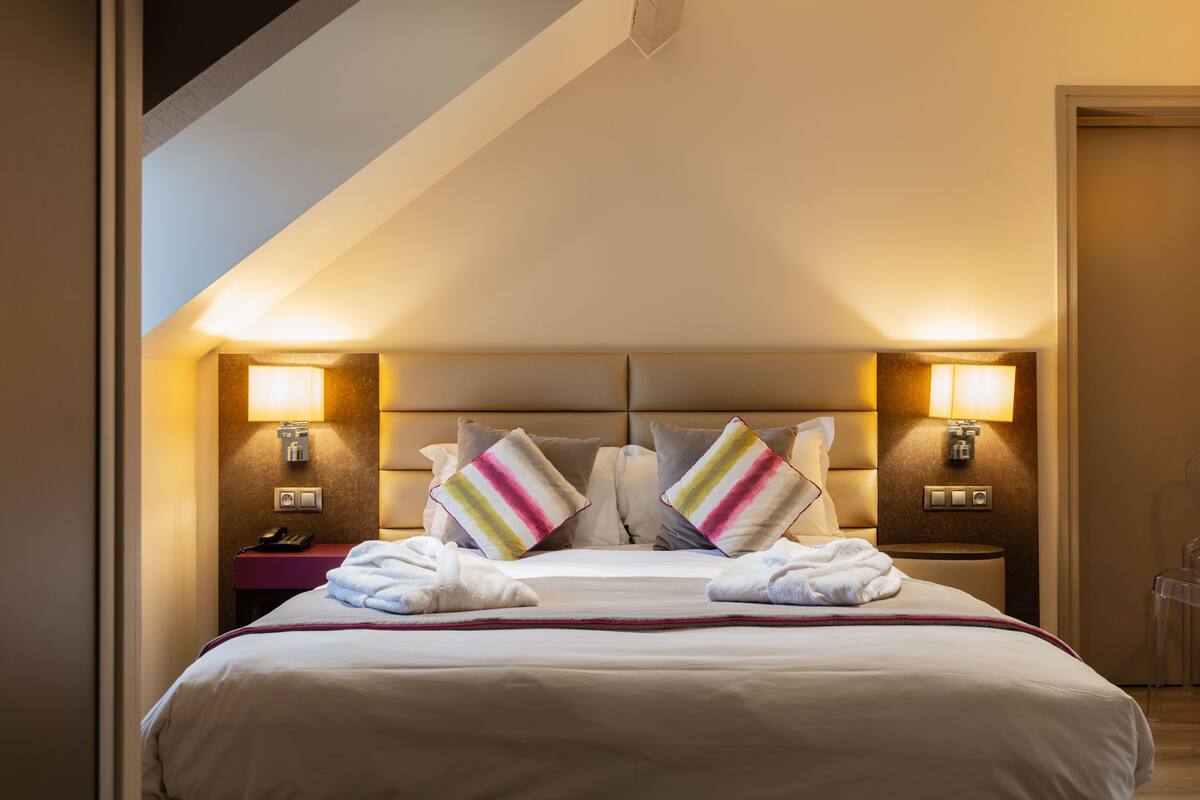 Quarto de hotel com uma cama grande, duas luminárias de cabeceira, um telefone e uma mesinha de cabeceira.