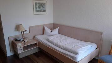 Uma cama de solteiro com estrutura de madeira, uma mesa de cabeceira com abajur e uma cadeira.