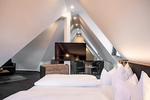 Quarto sótão moderno com formato triangular, cama, área de estar e televisão de tela plana.