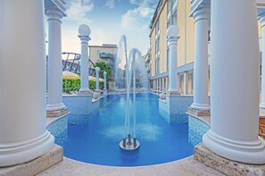 Uma área de piscina com uma fonte, rodeada por colunas brancas e um piso de azulejos.