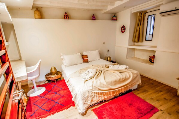 Quarto com cama, tapete vermelho, cadeira branca e objetos decorativos na parede.