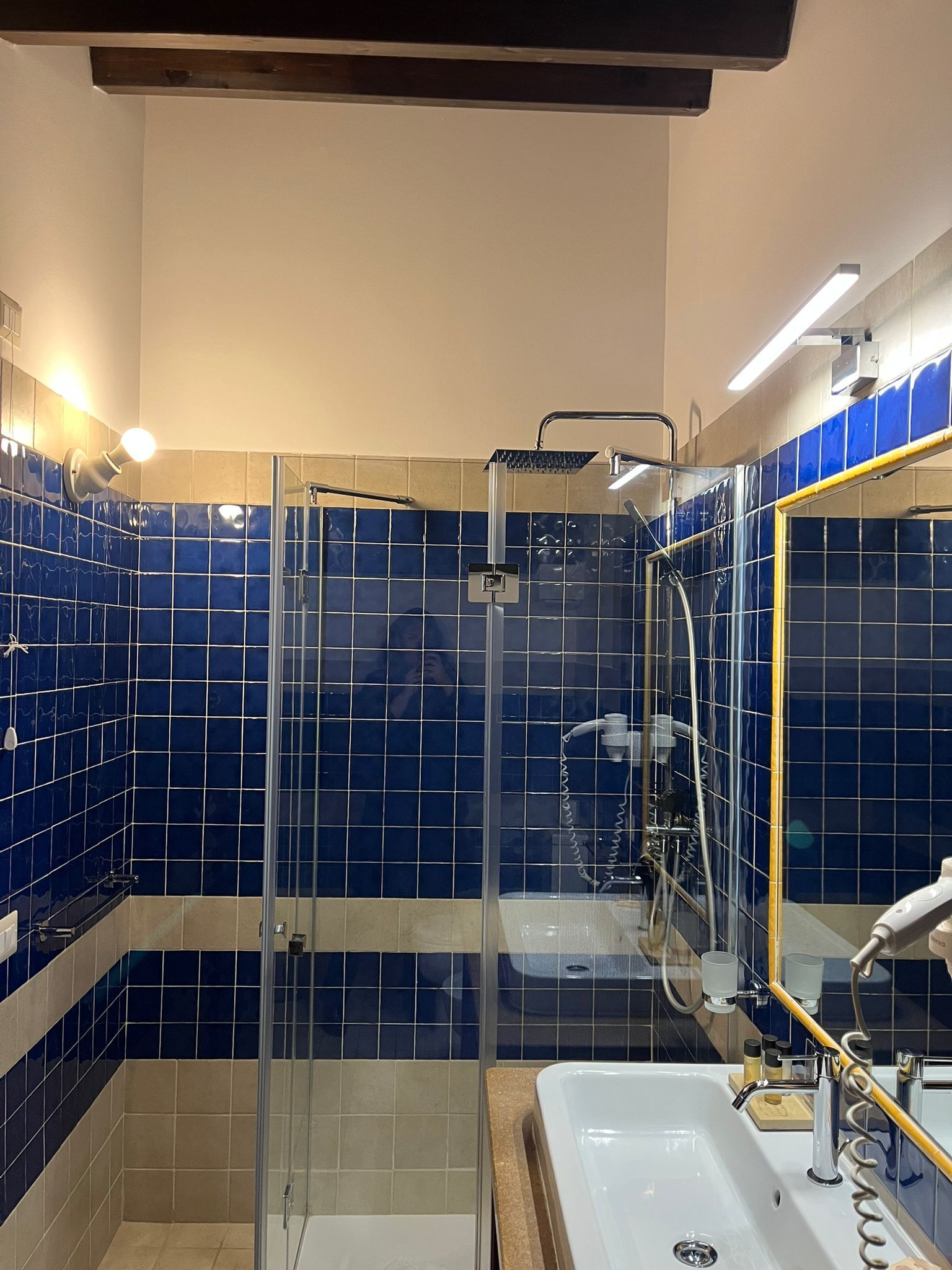 Casa de banho com chuveiro em cabine de vidro, lavatório branco e espelho com moldura dourada.