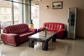 Um lobby moderno com sofás de couro, uma mesa de centro de vidro, uma máquina de refrigerantes Coca-Cola e grandes janelas com vista para a rua.