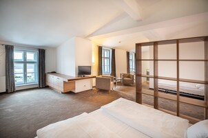 Quarto de hotel moderno com uma cama grande, uma escrivaninha com televisão, uma cadeira e vista para o exterior.