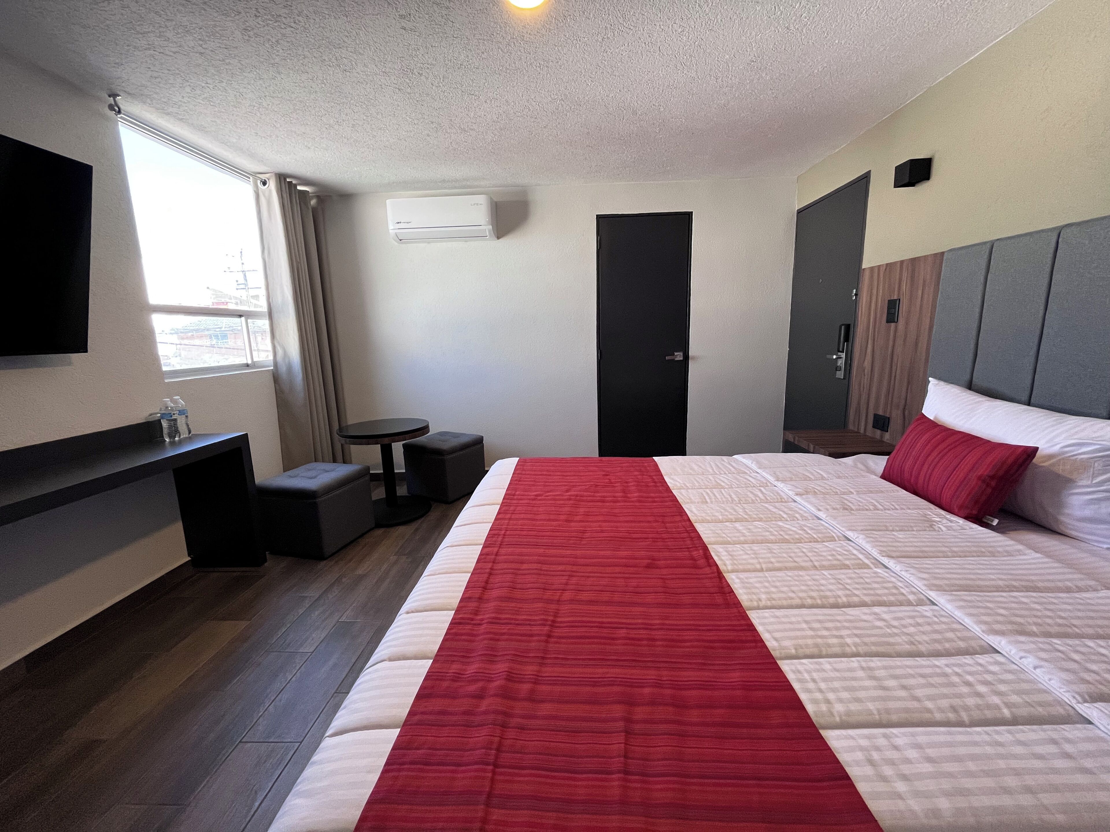 Quarto de hotel com cama, uma pequena mesa, uma cadeira, televisão e ar condicionado.