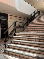Escada com corrimãos pretos e degraus bege, subindo para um andar superior.