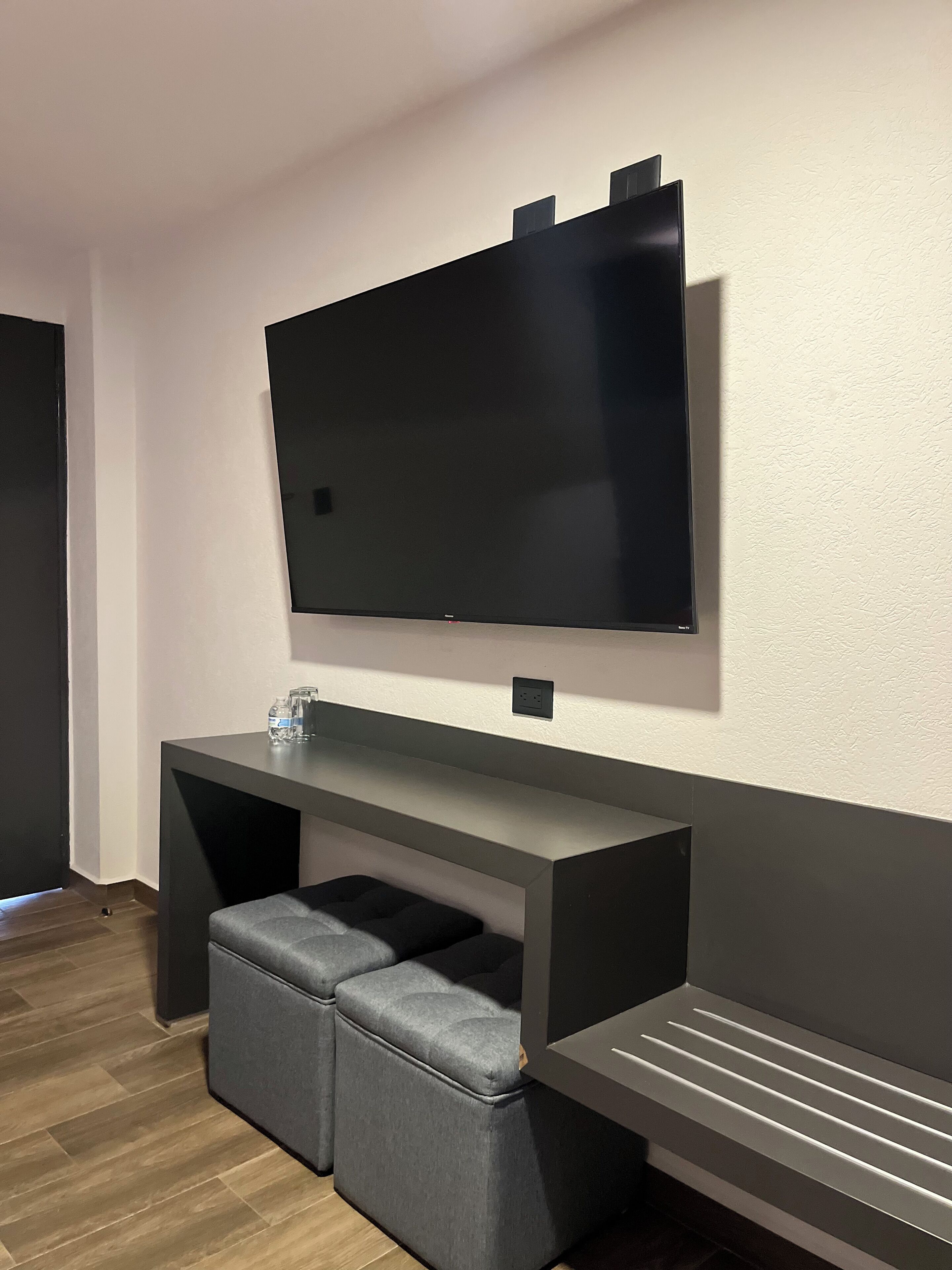 Uma sala de estar moderna com uma TV de tela plana na parede, um console escuro e um banco acolchoado cinza.
