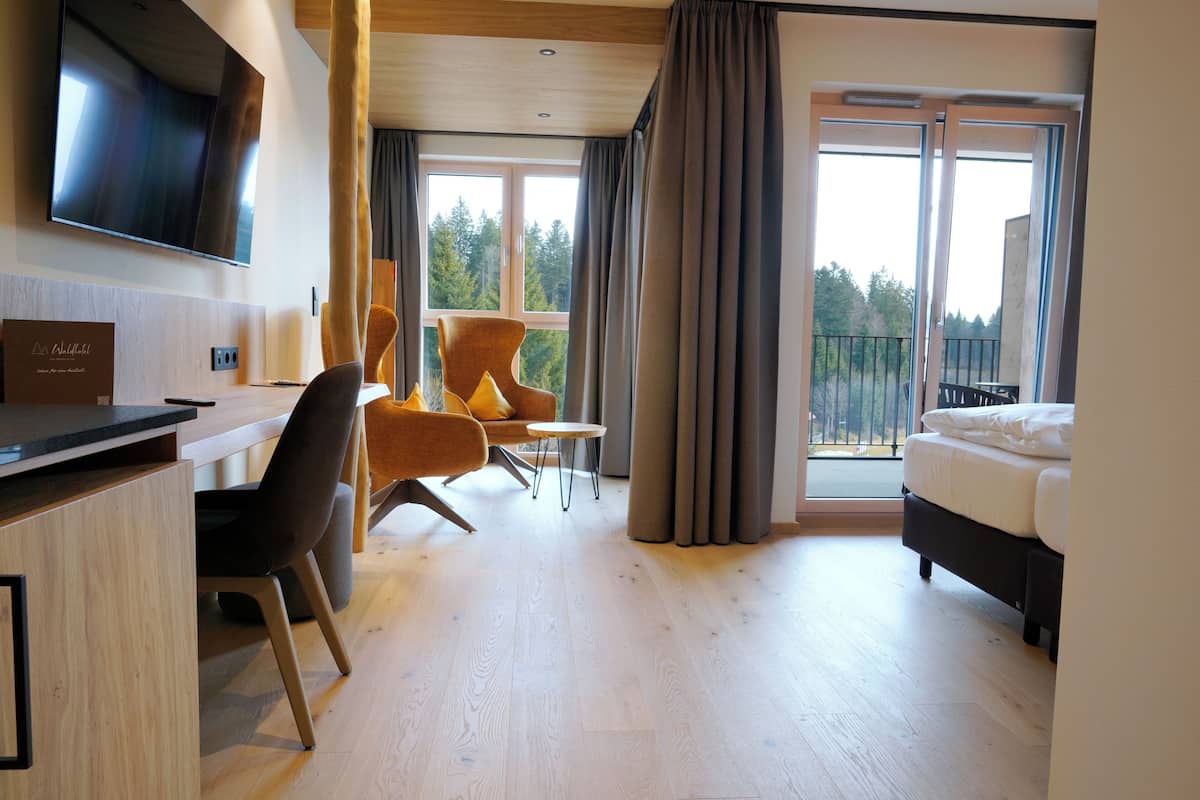 Quarto de hotel com cama, escrivaninha, cadeira, televisão e vista para o exterior.