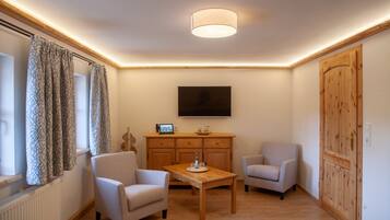 Quarto com duas poltronas, uma mesa de madeira, uma TV de tela plana, um armário de madeira e uma porta de madeira.