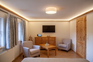 Quarto com duas poltronas, uma mesa de madeira, uma TV de tela plana, um armário de madeira e uma porta de madeira.