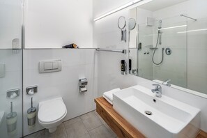 Uma casa de banho moderna com cabine de duche em vidro, lavatório branco e toucador de madeira.