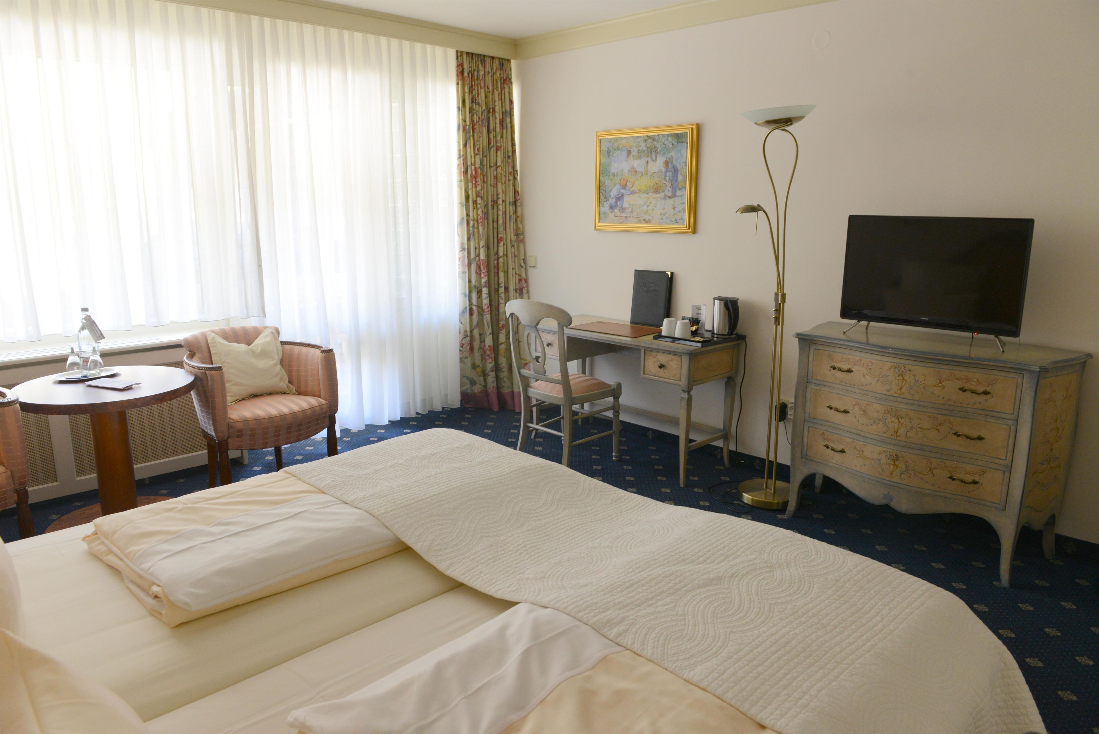 Quarto de hotel com cama, escrivaninha, cadeira, televisão e abajur.