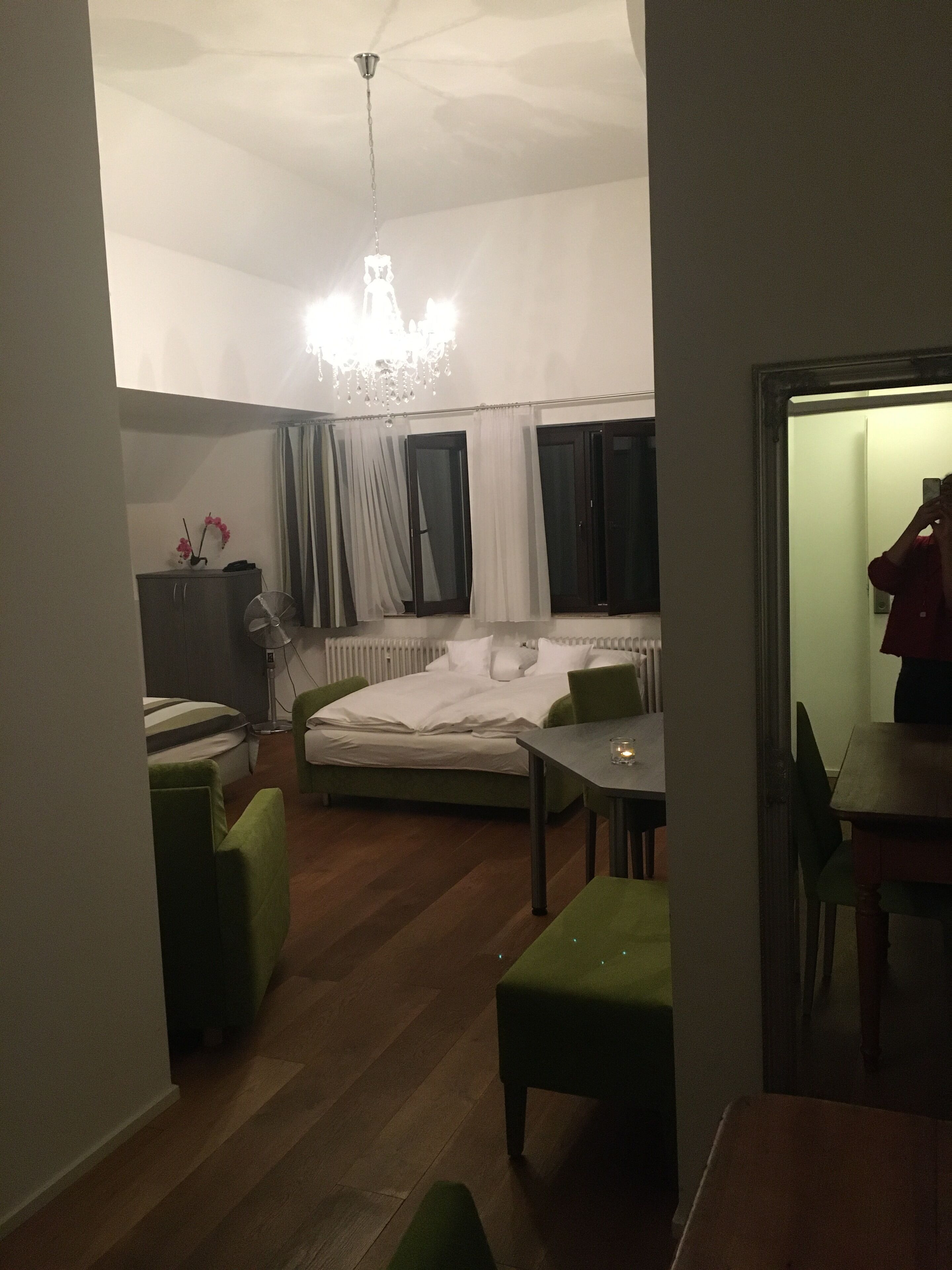 Quarto com cama, escrivaninha, cadeira, radiador e janela com cortinas.
