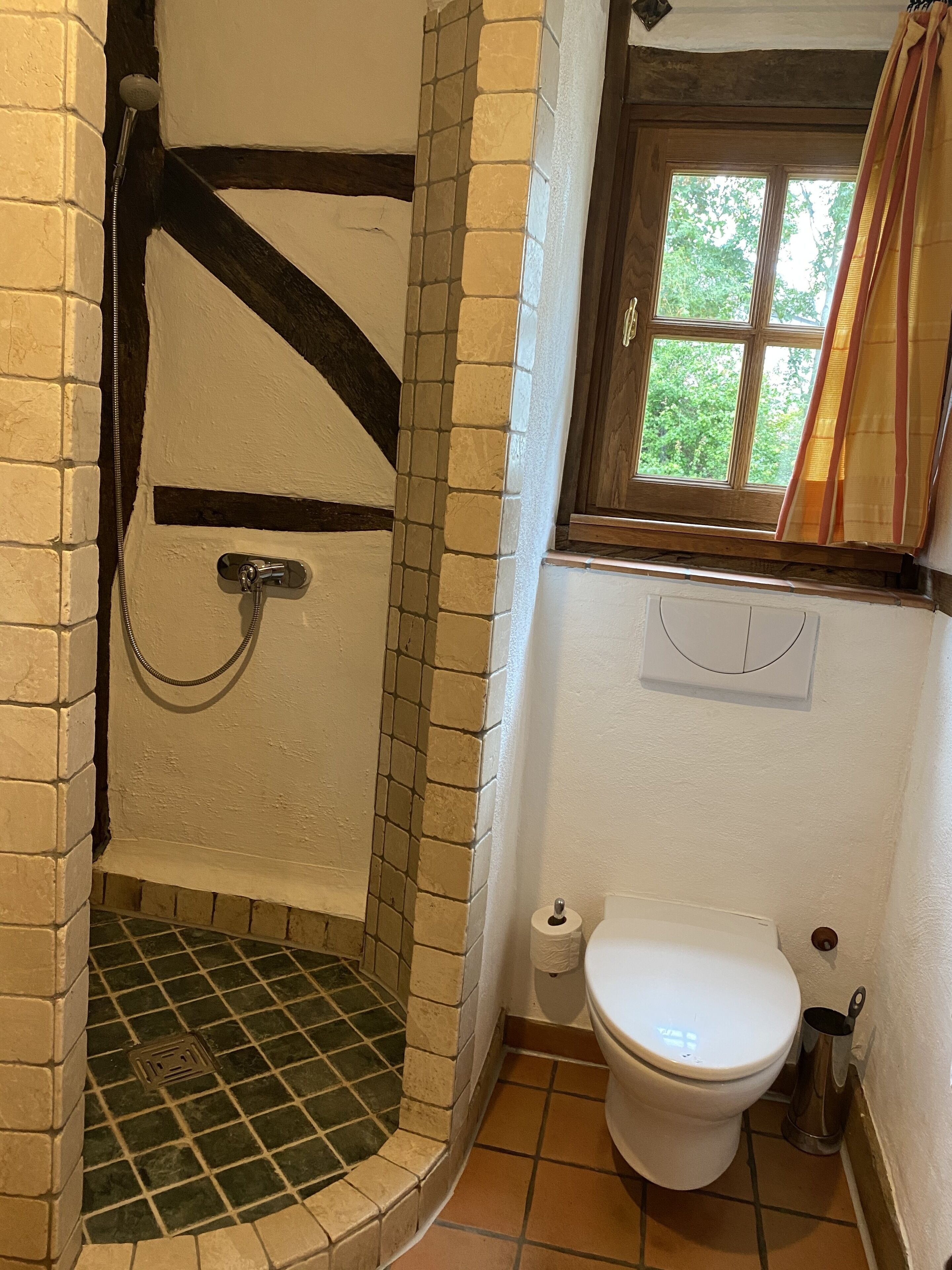 Um banheiro com chuveiro, vaso sanitário e janela com cortinas.