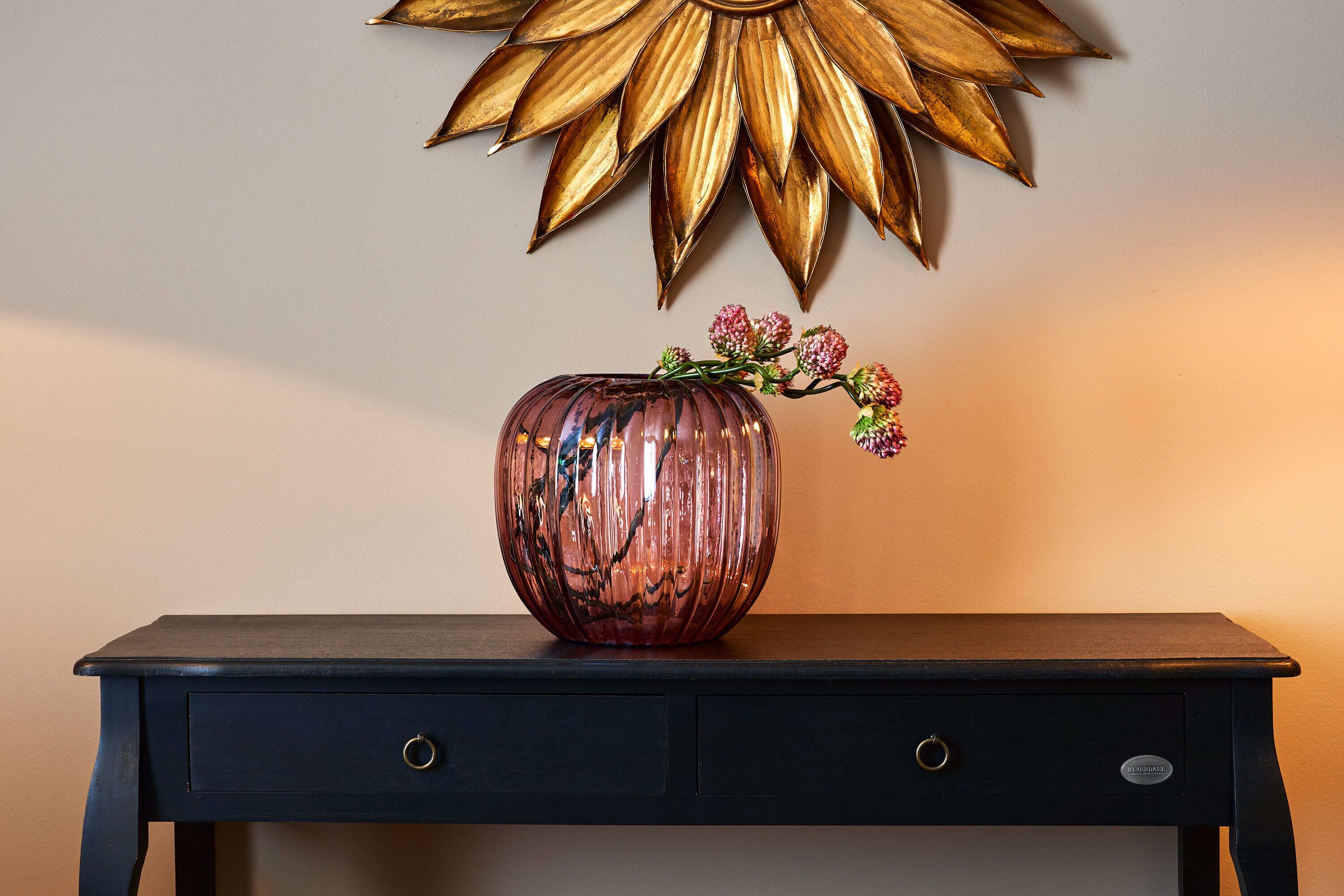 Uma mesa de madeira escura com um vaso decorativo com flores cor-de-rosa.