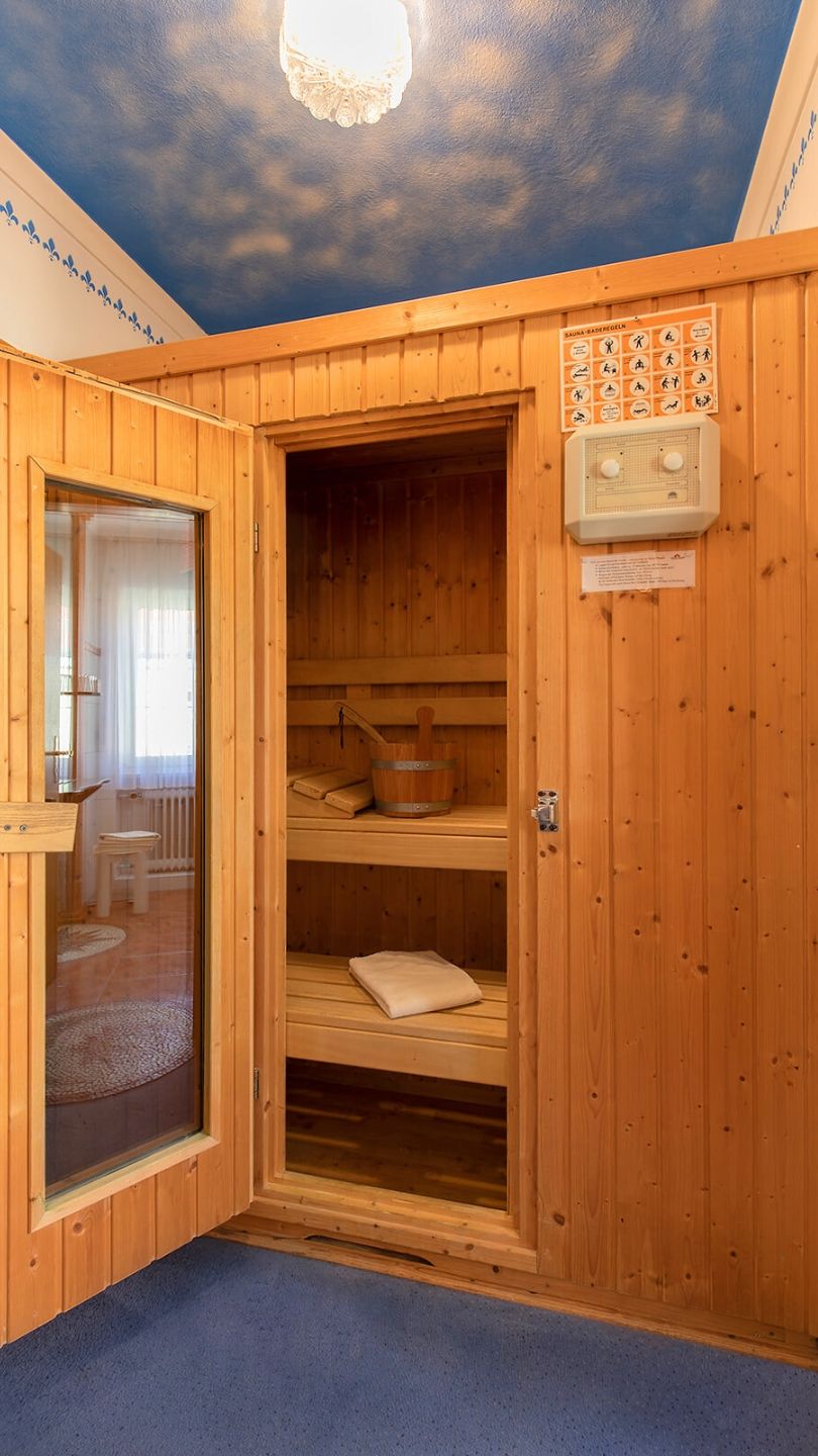 Uma sauna de madeira com porta de vidro, painel de controle e uma toalha no banco.