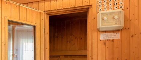 Uma sauna de madeira com porta de vidro, painel de controle e uma toalha no banco.