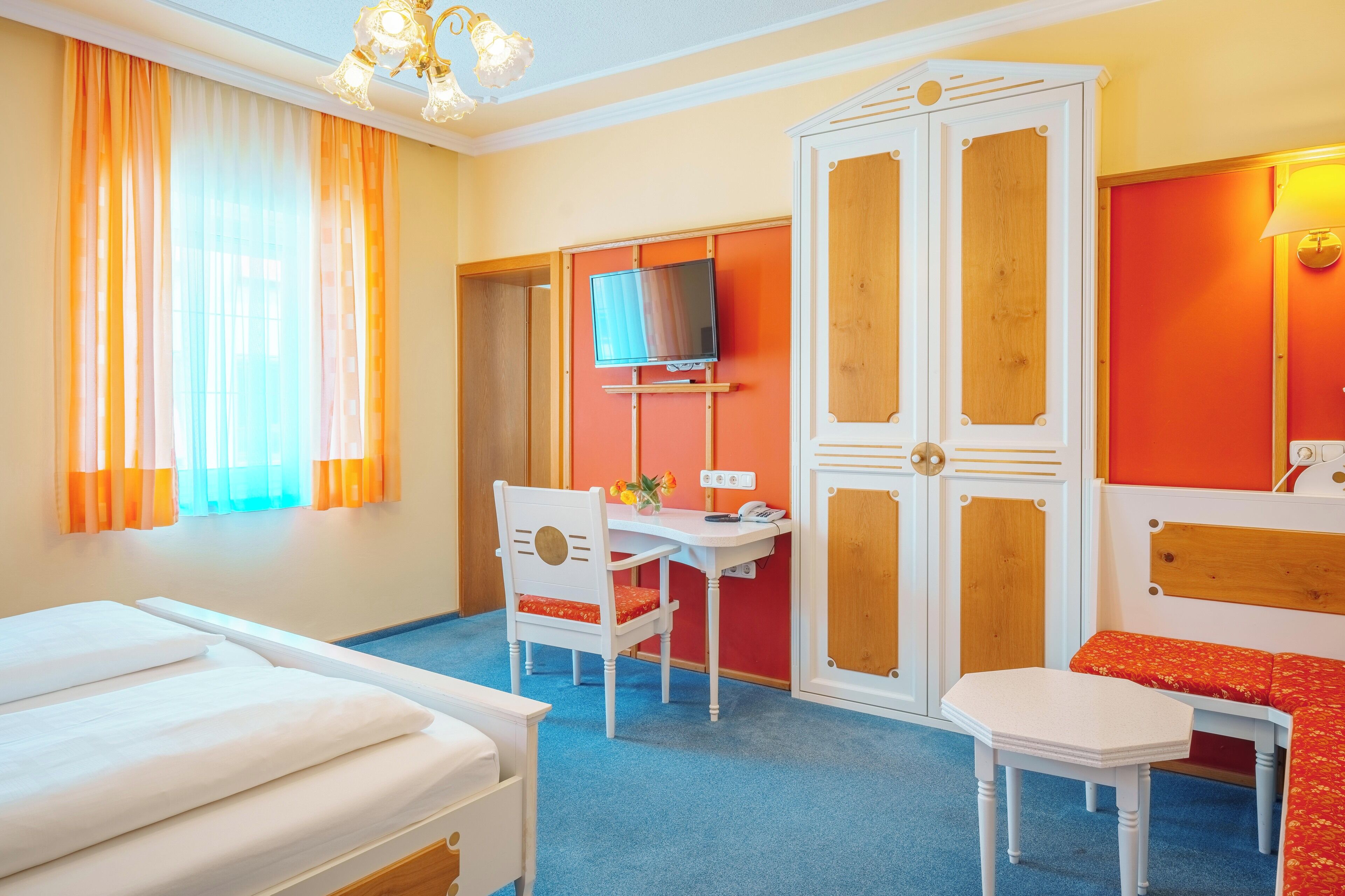 Quarto de hotel com duas camas, uma escrivaninha com cadeira, televisão e um guarda-roupa espaçoso.