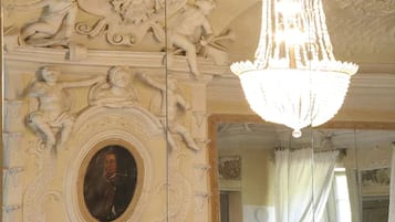 Um quarto com decorações elaboradas no teto, um candelabro e um retrato emoldurado em formato oval.