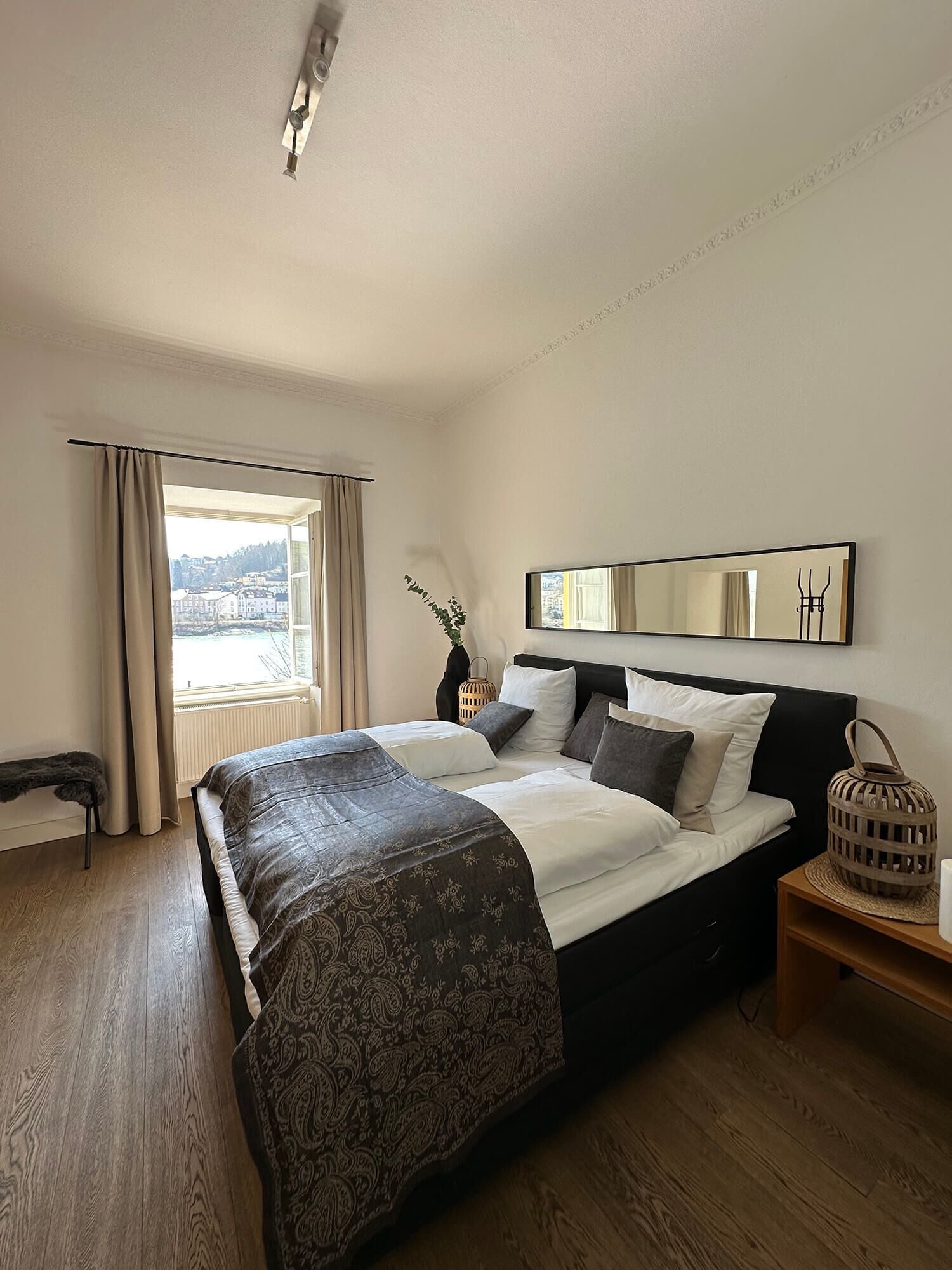Quarto com uma cama grande, mesa de cabeceira, janela com cortinas e vista para o exterior.