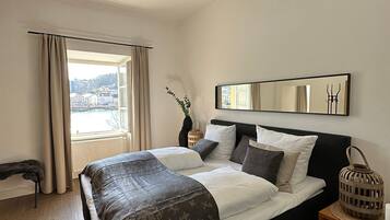 Quarto com uma cama grande, mesa de cabeceira, janela com cortinas e vista para o exterior.
