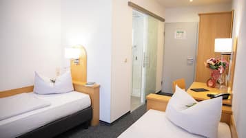 Quarto de hotel com duas camas, uma mesa, uma cadeira, um espelho e área de chuveiro.