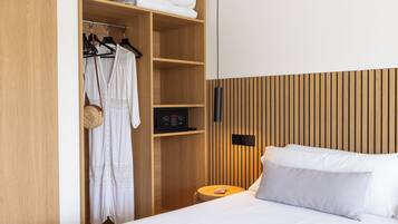 Quarto de hotel com cama, guarda-roupa de madeira, mesa de cabeceira pequena e painel de controle fixado na parede.