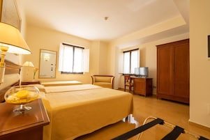 Quarto de hotel com duas camas, uma escrivaninha com televisão e um guarda-roupa.