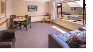 Quarto de hotel com área de refeições, sofá, televisão e janela com vista para edifícios.