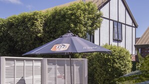 Um pátio externo com mesa e cadeiras, um guarda-sol azul e uma cerca branca.