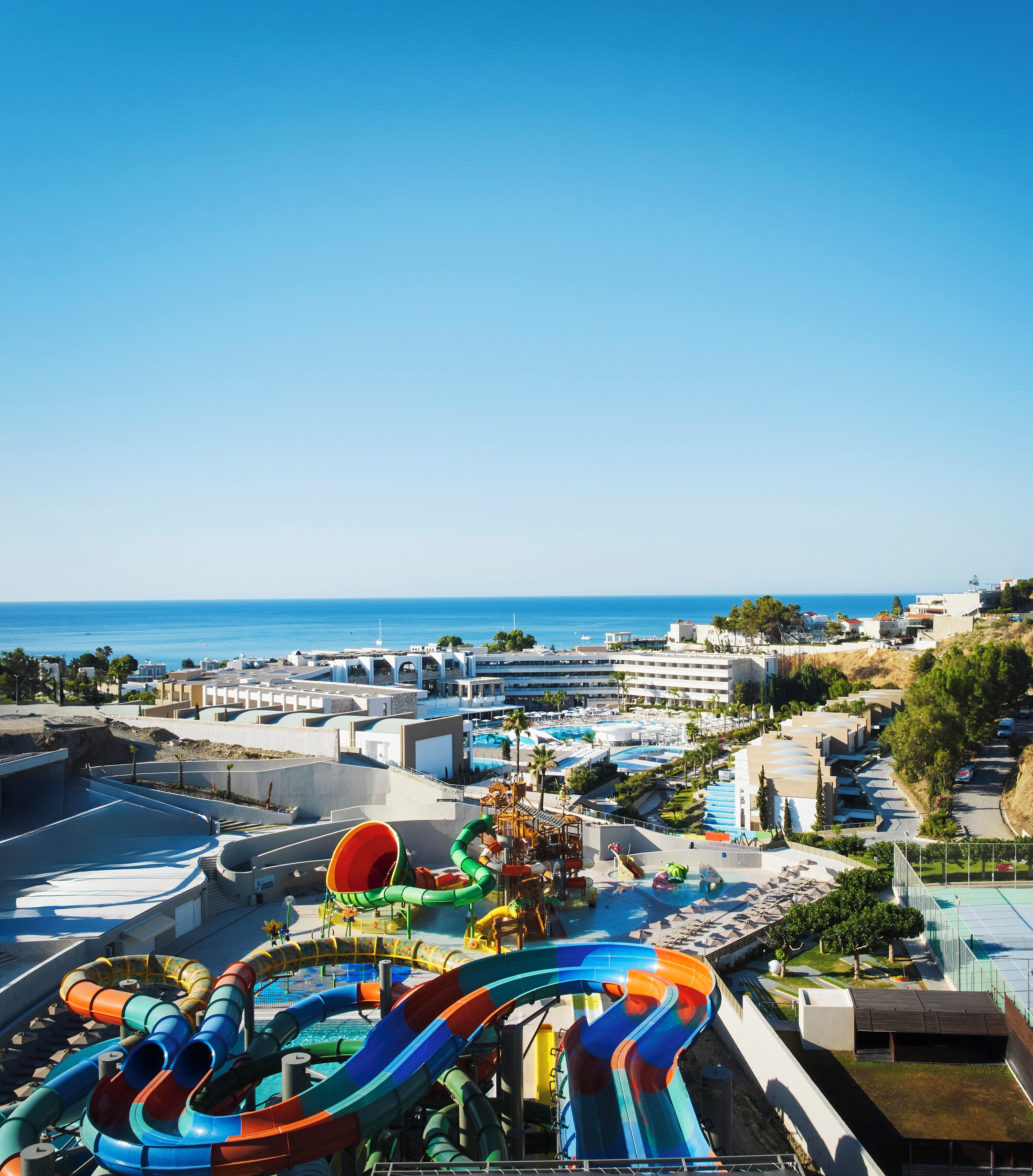Um parque aquático com vários toboáguas e área de piscina, cercado por edifícios e vista para o mar.