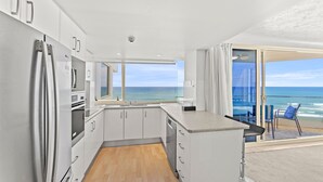 Uma cozinha moderna com vista para o oceano, uma varanda com assentos e uma porta de vidro deslizante.