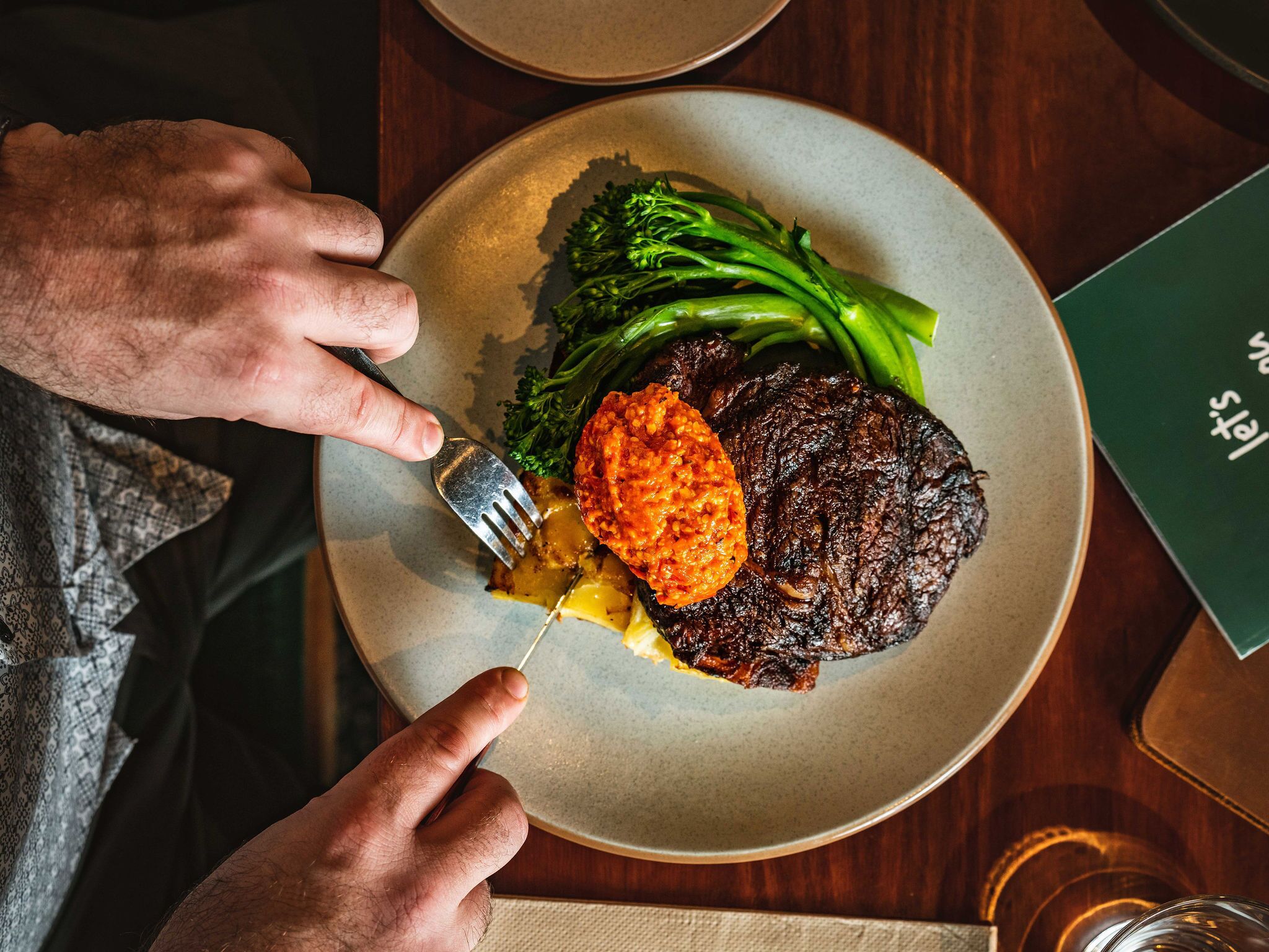Uma pessoa segurando um garfo sobre um prato com bife, brócolis e purê de batata.