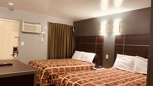 Quarto de hotel com duas camas, uma escrivaninha, ar condicionado, uma porta e cortina.