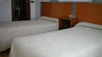 Duas camas de solteiro com cabeceiras, uma mesa de cabeceira com telefone e uma pequena prateleira.