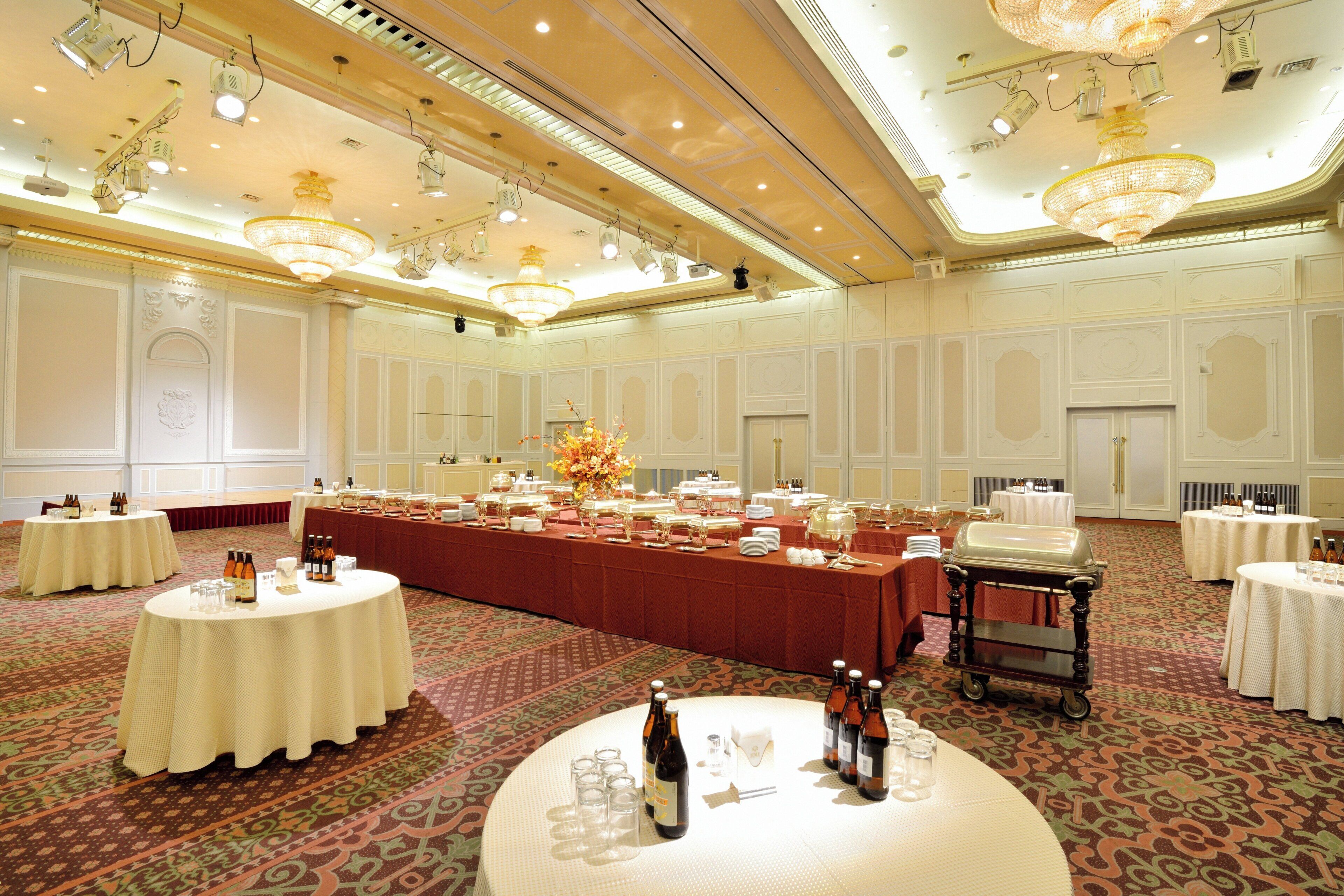 Uma sala de banquetes com mesas redondas, uma longa mesa de banquete e um candelabro.
