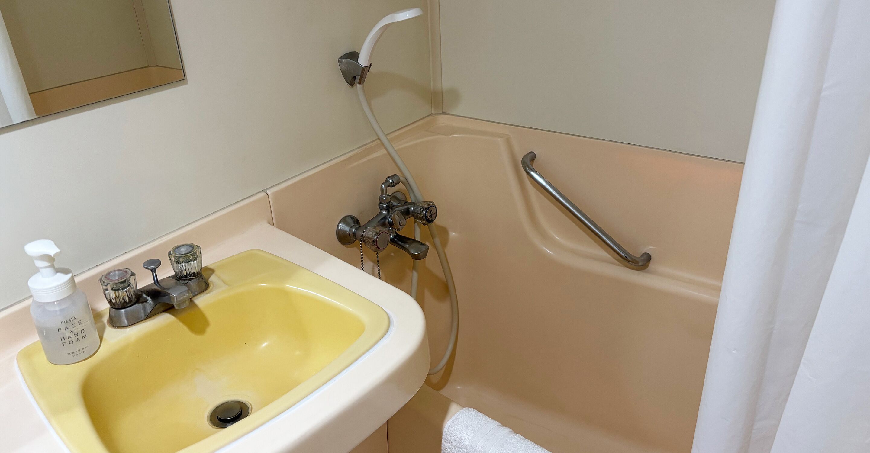 Casa de banho com lavatório amarelo, espelho, chuveiro manual e barra de apoio.