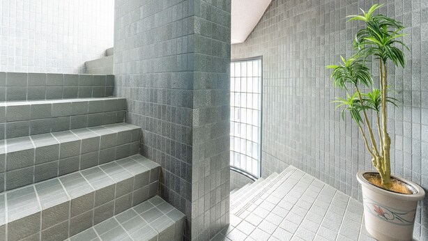 Interior moderno com paredes de azulejos cinzas, um vaso de planta e uma janela.