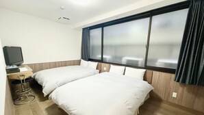 Quarto de hotel com duas camas, uma escrivaninha com televisão e uma janela grande com cortinas.