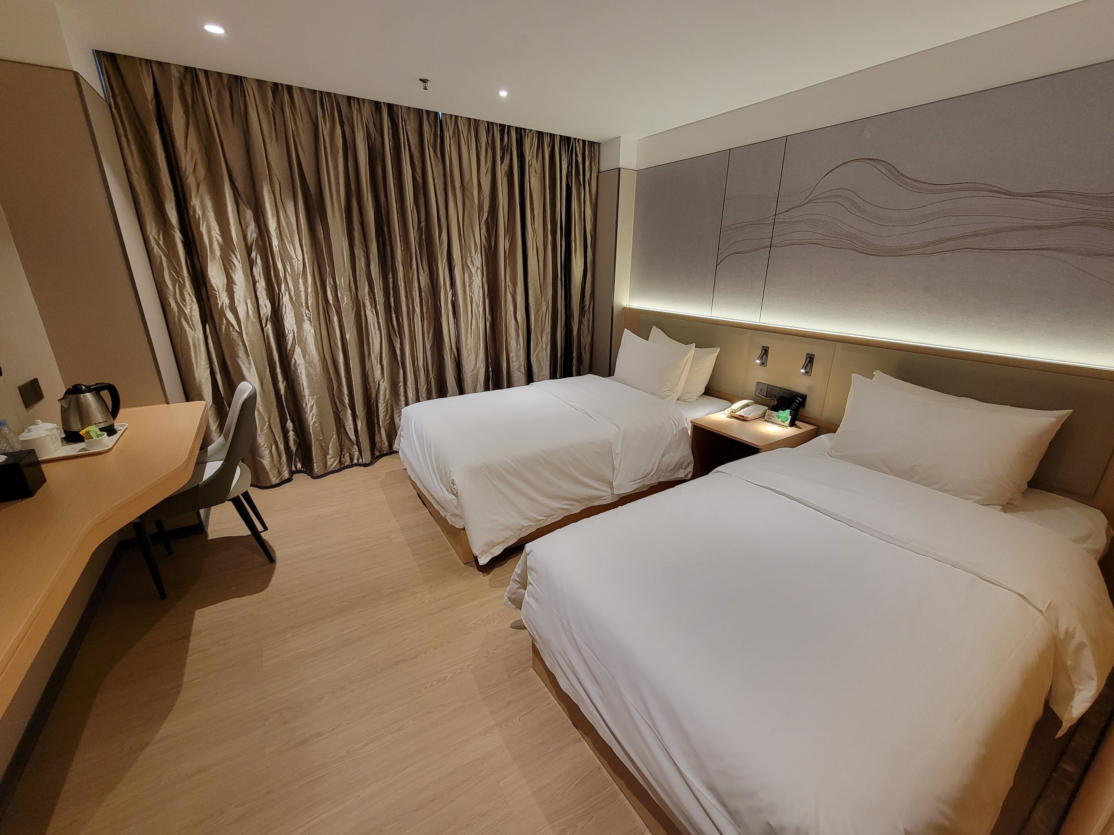Quarto de hotel com duas camas, uma escrivaninha, uma cadeira, uma cafeteira e um telefone.