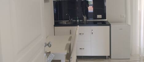 Uma cozinha compacta com micro-ondas embutido, pequena geladeira e televisão de tela plana fixada acima do balcão.