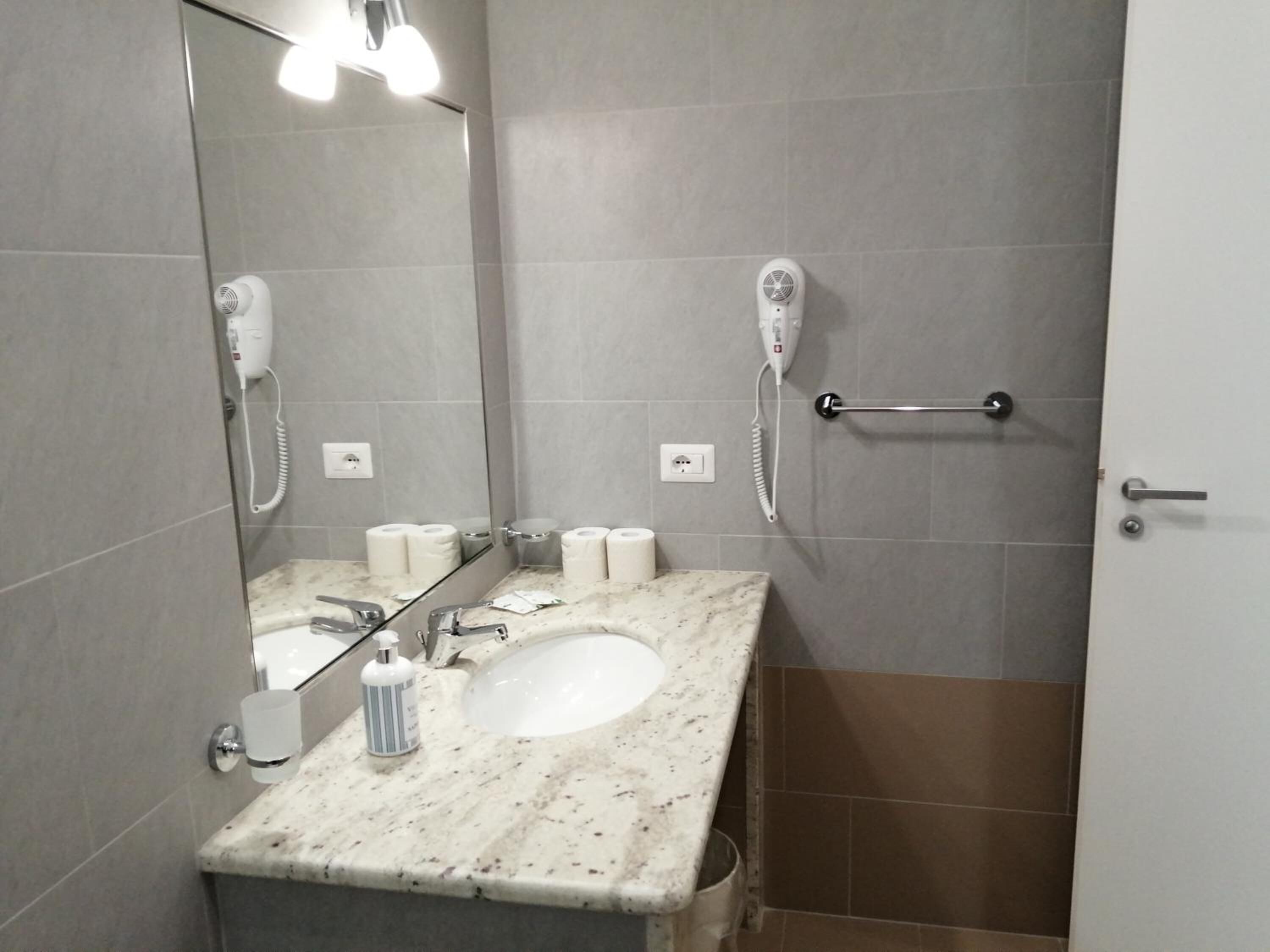 Casa de banho com lavatório de mármore, espelho, dois secadores de cabelo e um porta-toalhas.